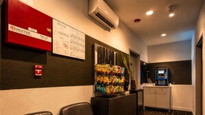Uma área de recepção de hotel com balcão de check-in, detector de incêndio, máquina de venda automática e área de estar com poltronas de couro.