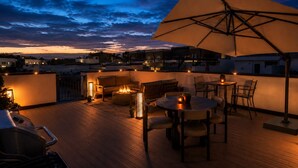 Terraço no telhado com área de refeições, churrasqueira e um grande guarda-sol para proteção contra o sol.