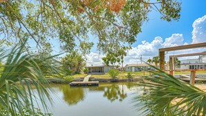 Uma área externa tranquila com lago, deck de madeira e vegetação exuberante ao redor.