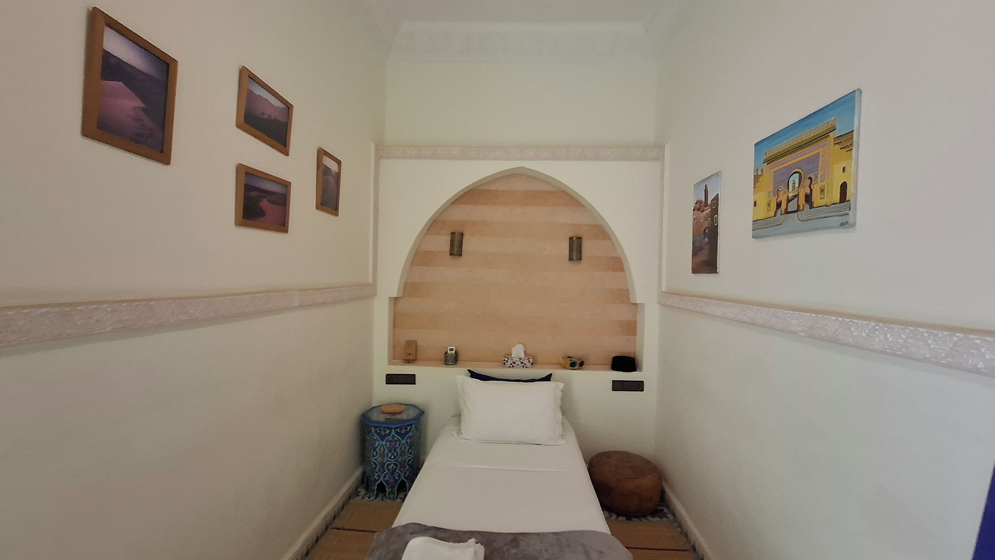 Quarto de hotel pequeno com cabeceira de madeira, cama, mesa de cabeceira e prateleira fixada na parede.