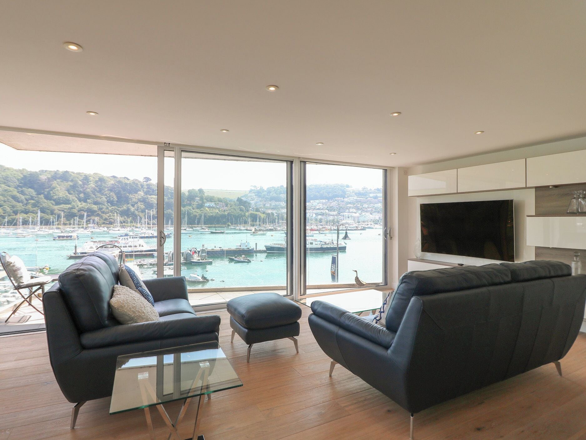 Uma sala de estar moderna com uma televisão grande, assentos confortáveis e vista para uma marina.