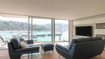 Uma sala de estar moderna com uma televisão grande, assentos confortáveis e vista para uma marina.