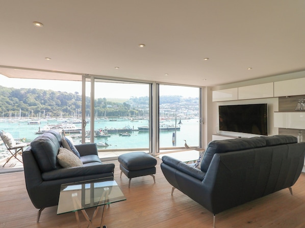 Uma sala de estar moderna com uma televisão grande, assentos confortáveis e vista para uma marina.