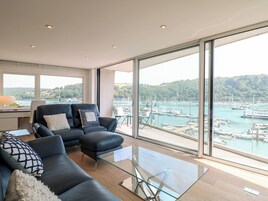 Uma sala de estar moderna com uma mesa de centro de vidro, um sofá de couro preto e vista para um porto de iates.