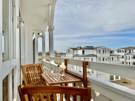 Varanda com mesa e cadeiras de madeira, com vista para uma fileira de edifícios brancos com varandas.