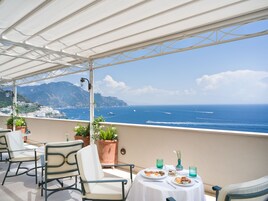 Um terraço com área de estar ao ar livre, mesa posta para o café da manhã e vista para o mar e montanhas.