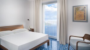 Quarto de hotel com cama, cadeira, quadro, janela com cortinas e luminária no teto.