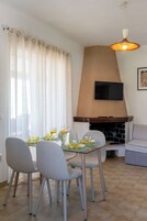 Uma sala de jantar com uma mesa posta para quatro pessoas, uma televisão montada sobre a lareira e um sofá ao fundo.