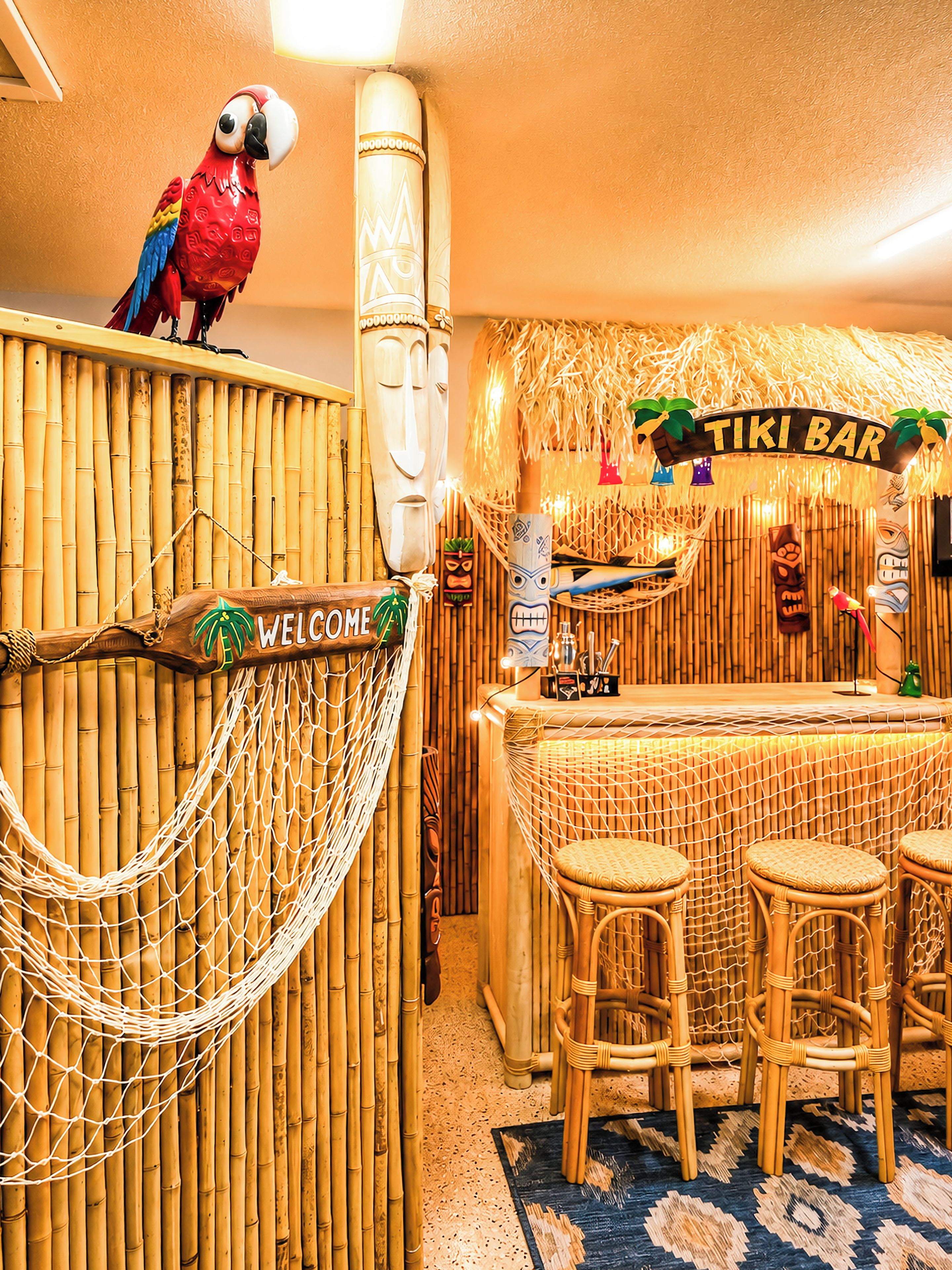 Um bar tiki com decoração em madeira, uma placa de boas-vindas e um papagaio.