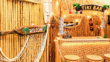 Um bar tiki com decoração em madeira, uma placa de boas-vindas e um papagaio.