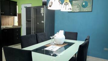 Uma sala de jantar com uma mesa posta para dois, geladeira e luminária fixada na parede.