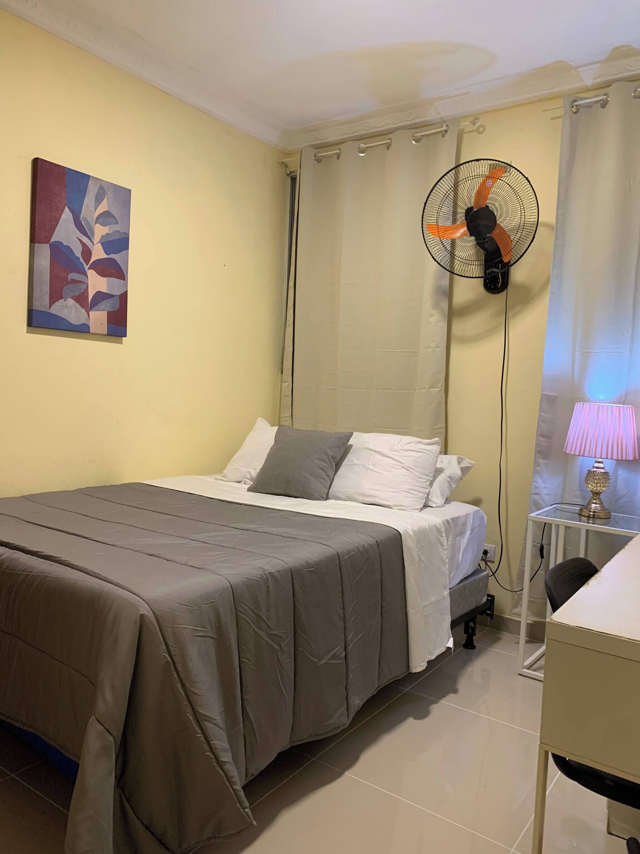 Quarto com cama, ventilador, luminária e uma pintura na parede.