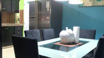 Uma área de refeições com mesa de vidro, cadeiras pretas e luminárias pendentes.