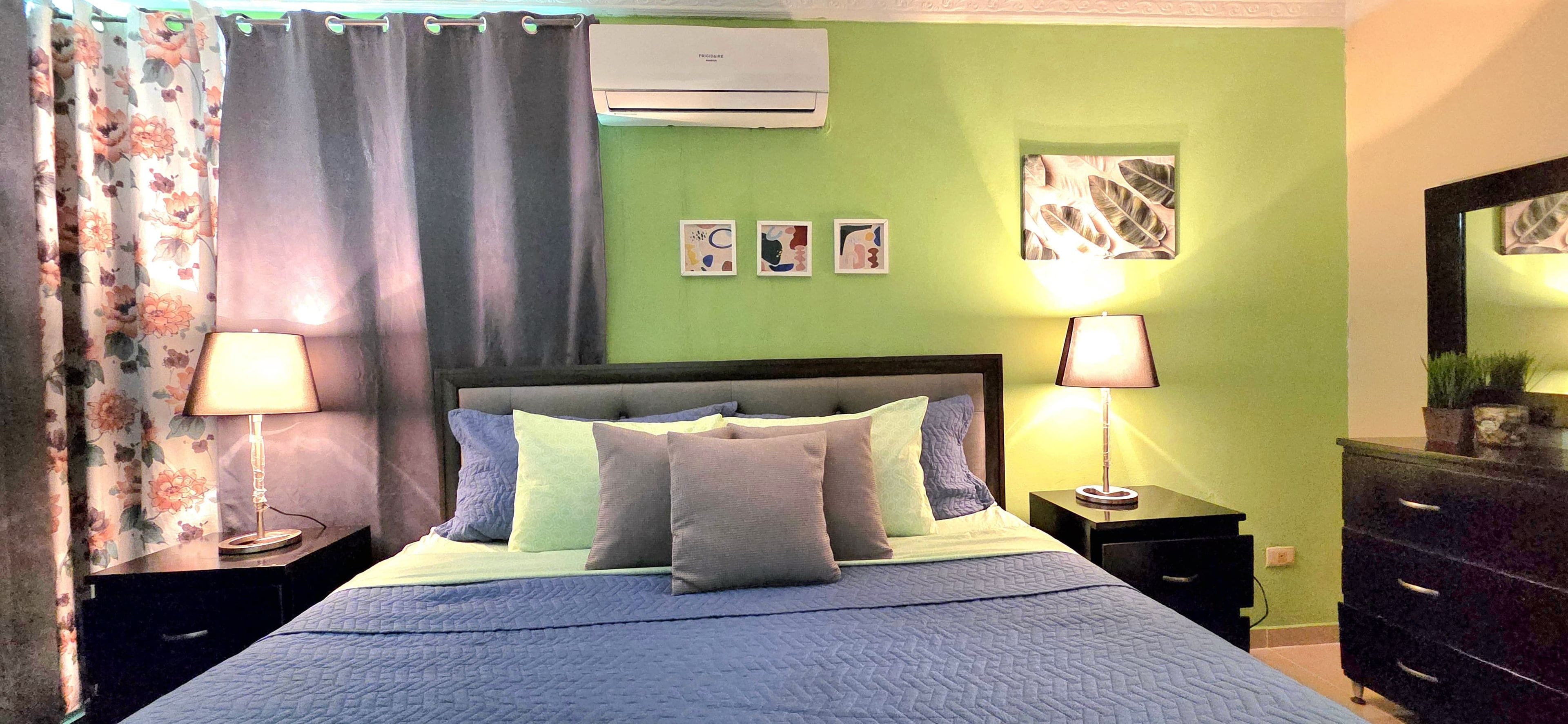 Quarto com cama, duas mesas de cabeceira com luminárias, ar-condicionado na parede e um espelho.