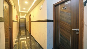Corredor de hotel com portas de madeira, placas com números e chão de mármore.