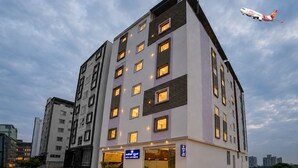 Um edifício de hotel moderno, com vários andares, uma entrada visível e uma placa indicando ser um hotel.