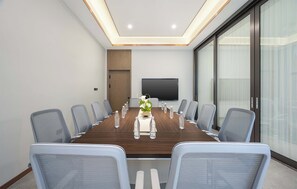 Uma sala de conferências com uma mesa comprida, cadeiras, uma tela de TV e um painel de vidro.