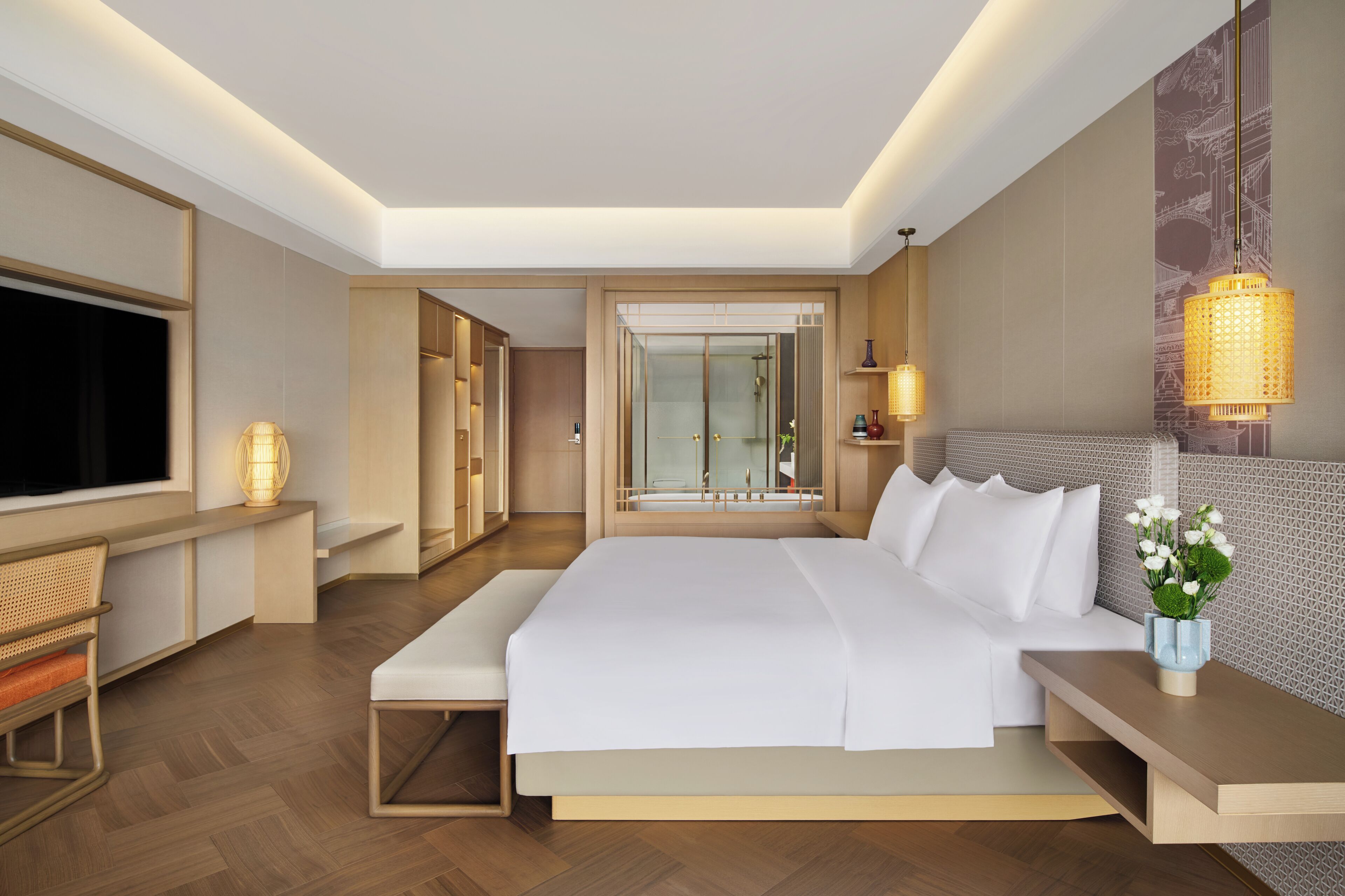 Quarto de hotel moderno com uma cama grande, televisão, escrivaninha e banheiro com porta de vidro.