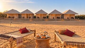 Resort no deserto com várias tendas, redes e uma mesa de vime com comida e bebidas.