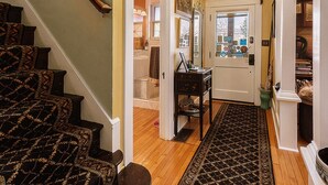 Uma escadaria que leva a um quarto com piso de madeira, uma porta com janela e uma pequena mesa com abajur.