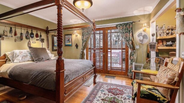 Uma cama com dossel, uma cadeira de madeira, um ventilador e uma janela com cortinas.