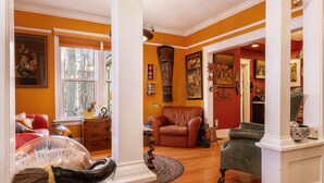 Um quarto com piso de madeira, um sofá de couro vermelho, uma poltrona verde e uma cadeira de couro marrom.