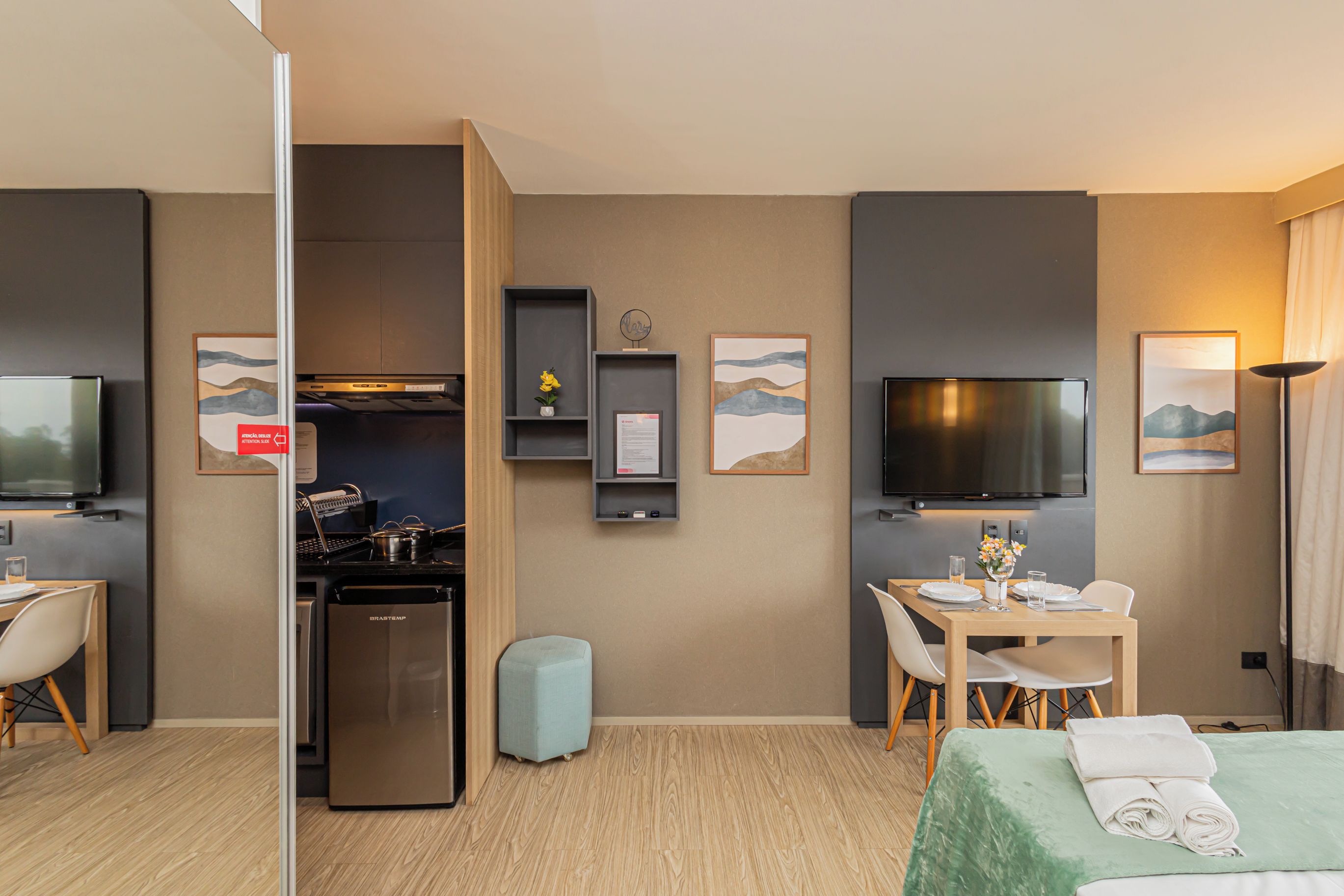 Quarto de hotel com cozinha compacta, área de refeições, cama e televisão.