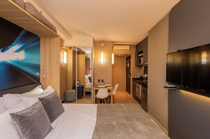 Quarto de hotel com uma cama, uma escrivaninha, uma mesa de jantar e uma televisão.