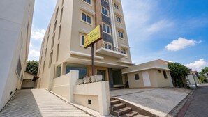 Um hotel de vários andares com uma placa de destaque, uma escadaria que leva à entrada e um céu claro.