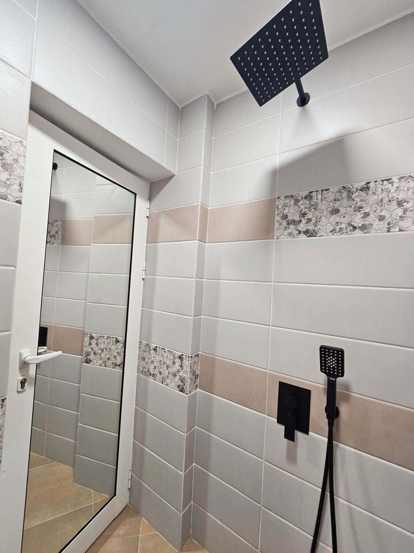 Casa de banho com azulejos brancos, um chuveiro e uma porta.