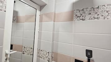 Casa de banho com azulejos brancos, um chuveiro e uma porta.