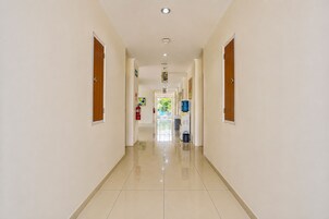 Corredor de hotel com portas em ambos os lados, piso ladrilhado e teto com iluminação embutida.