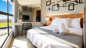 Quarto de hotel com cama, escrivaninha, cadeira, televisão e vista para um trem na janela.
