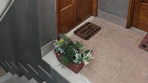 Uma porta dupla de madeira com uma placa, um pequeno vaso de planta e um tapete de entrada com uma mensagem.