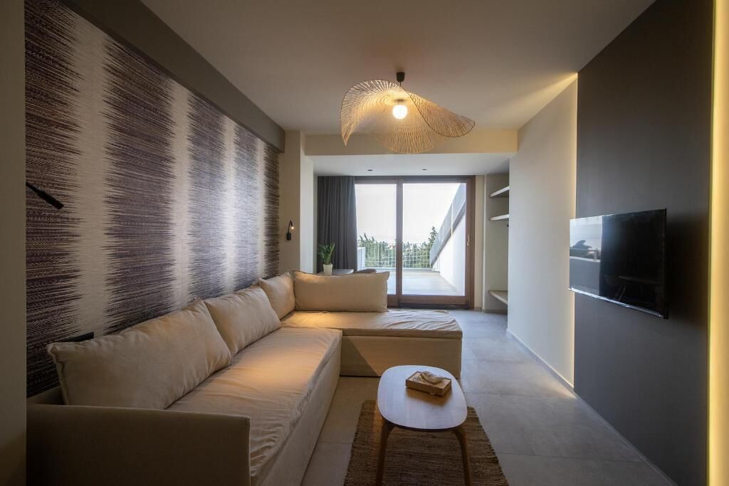 Uma sala de estar moderna com um sofá, uma mesa de centro, uma TV na parede e uma grande janela com vista.