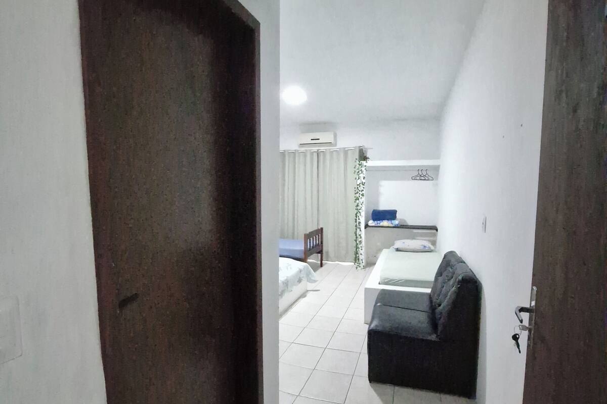 Quarto com cama, sofá, uma mesinha e janela com cortinas.