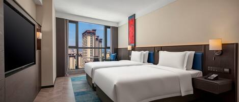 Quarto de hotel com uma cama grande, televisão, escrivaninha com telefone e vista para a paisagem urbana.