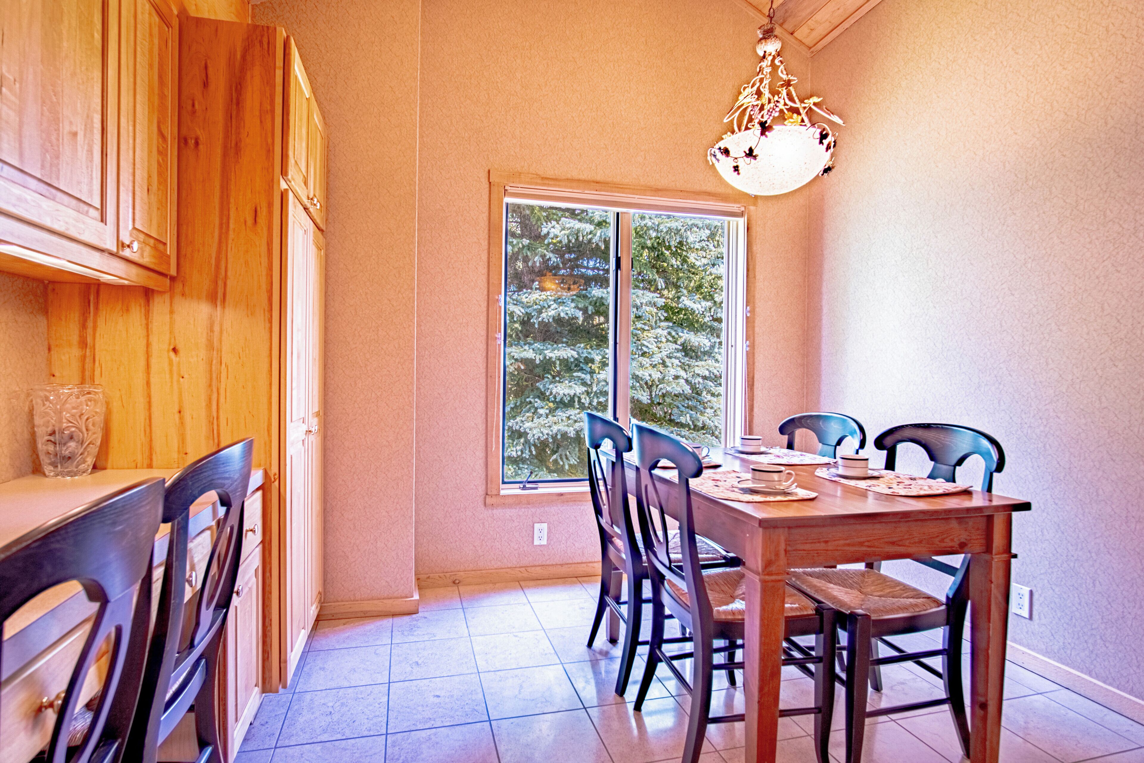 Uma sala de jantar com mesa de madeira, cadeiras e janela com vista para árvores.