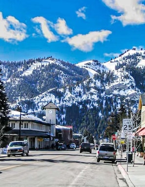 Uma cidade com uma torre do relógio, um sinal de limite de velocidade e montanhas cobertas de neve ao fundo.