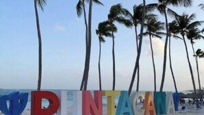 Uma praia com palmeiras e uma placa colorida com a palavra 'PUNTA CANA'.