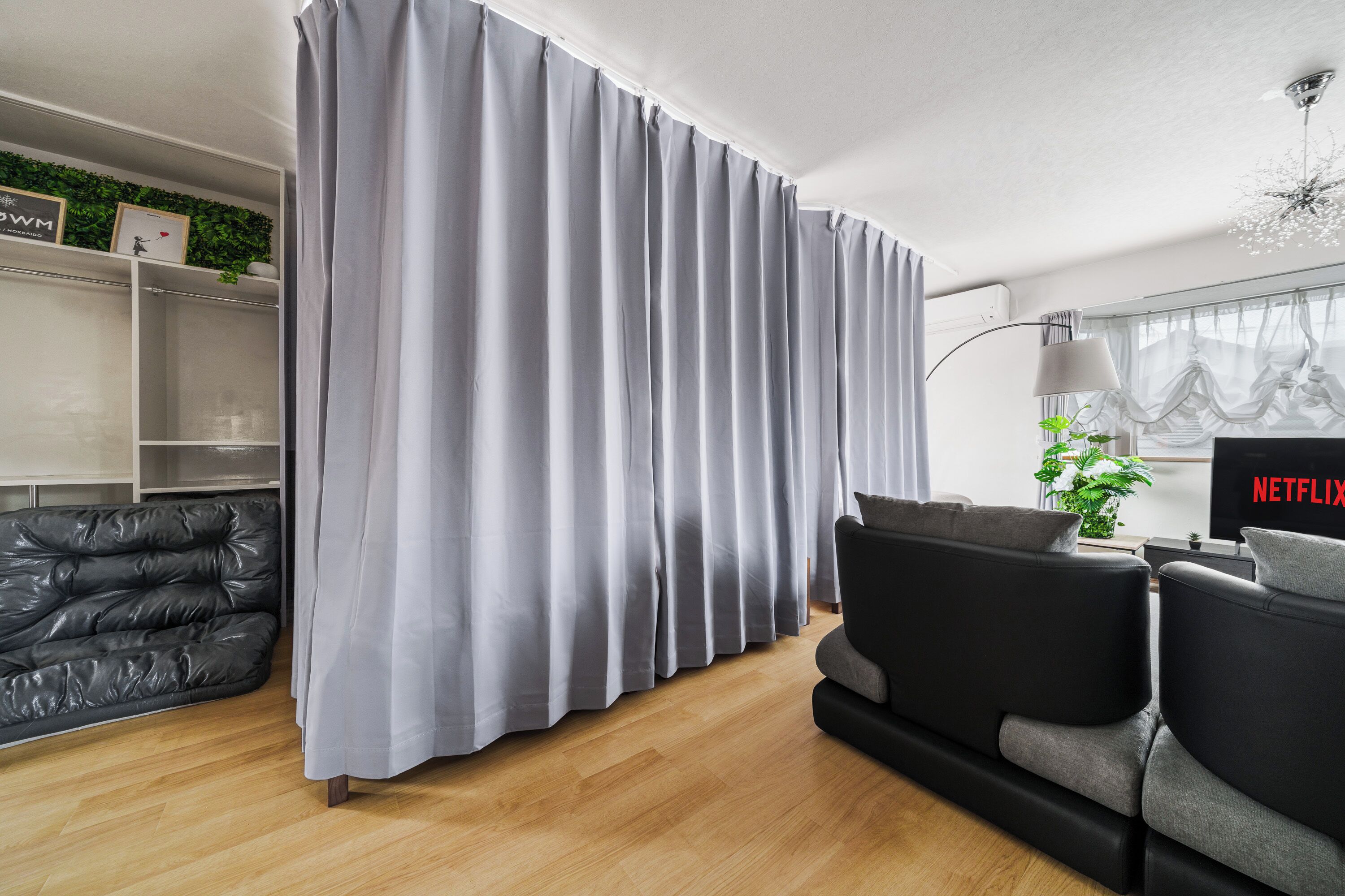 Uma sala de estar moderna com um sofá, uma poltrona de couro preto, uma televisão e uma cortina.