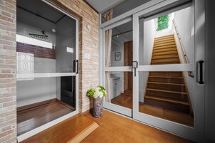 Interior moderno com parede de tijolos, escada de madeira e porta de vidro que dá para um banheiro.