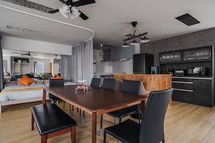 Um espaço moderno com sala de jantar, cozinha e uma cama grande com almofadas laranja.