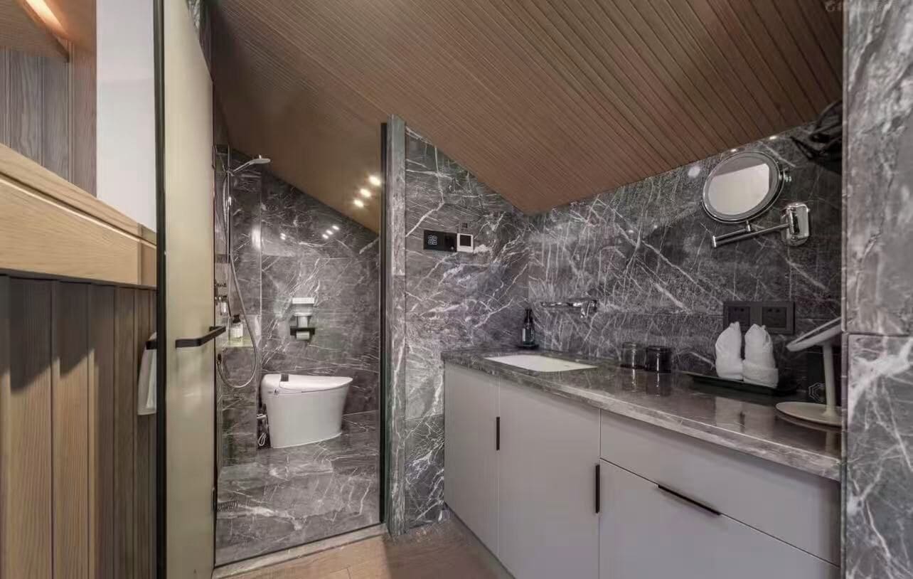 Um banheiro moderno com parede de mármore, pia, espelho e vaso sanitário.