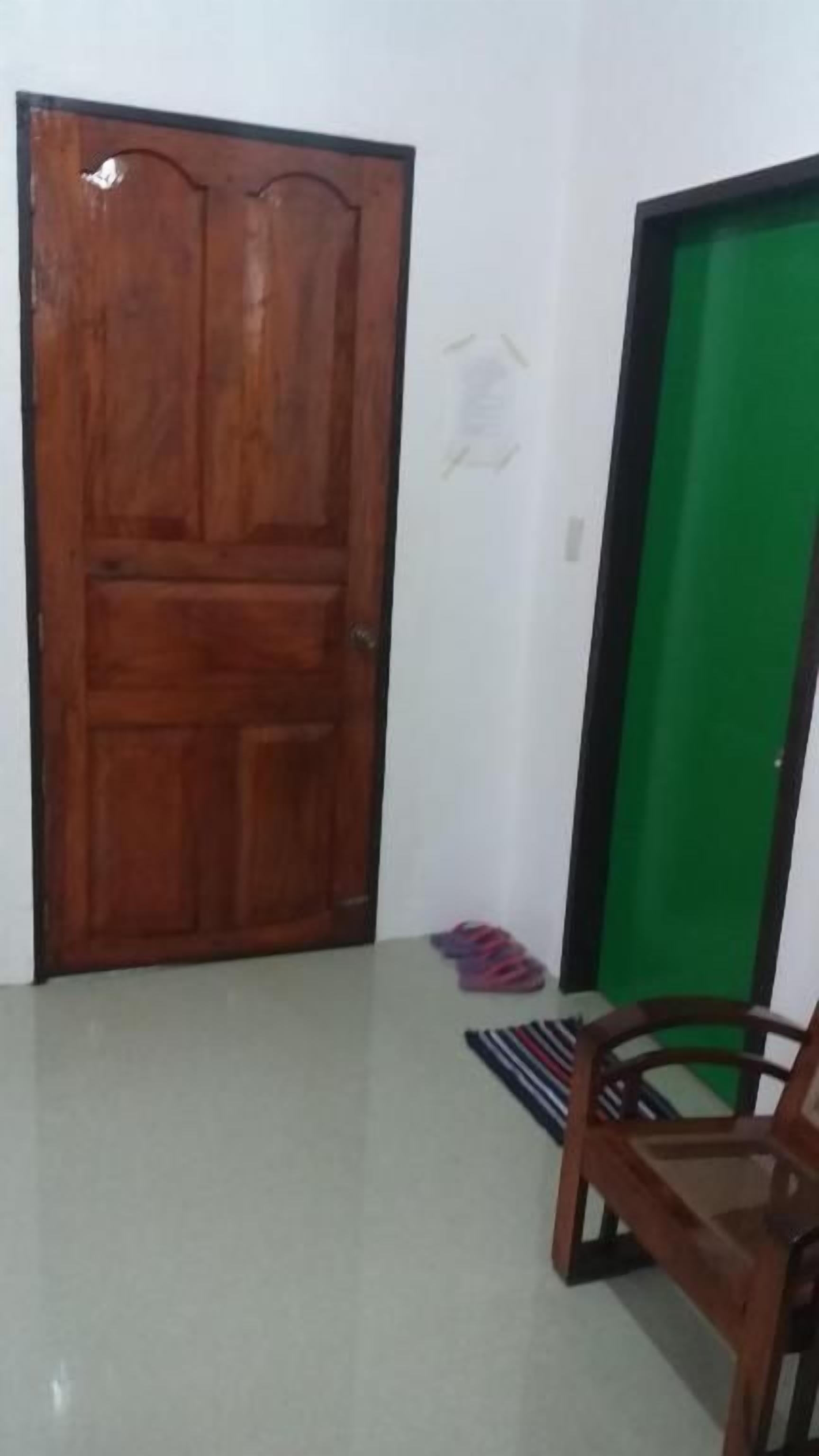 Um quarto com porta de madeira, porta verde, uma cadeira e um tapete no chão.