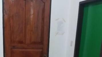 Um quarto com porta de madeira, porta verde, uma cadeira e um tapete no chão.