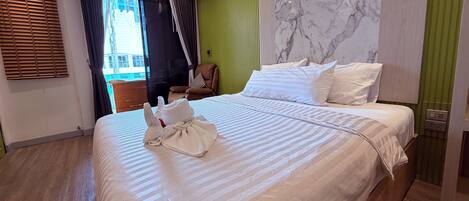 Quarto de hotel com uma cama grande, uma parede de destaque verde e vista para a cidade pela janela.
