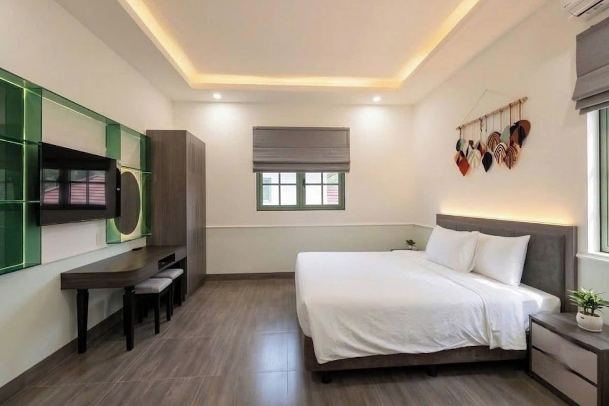 Quarto moderno com cama, escrivaninha e televisão fixada na parede.
