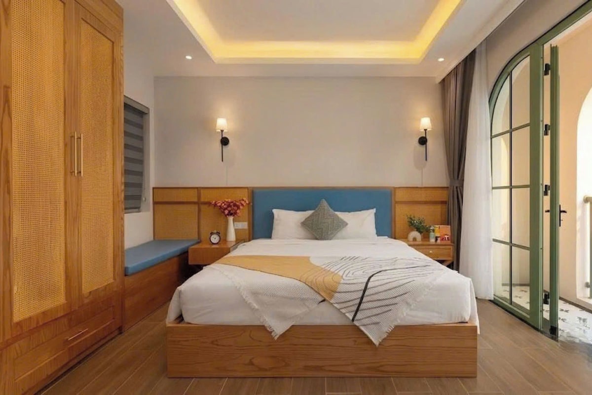 Quarto moderno com cama de madeira, mesas de cabeceira e uma janela grande.