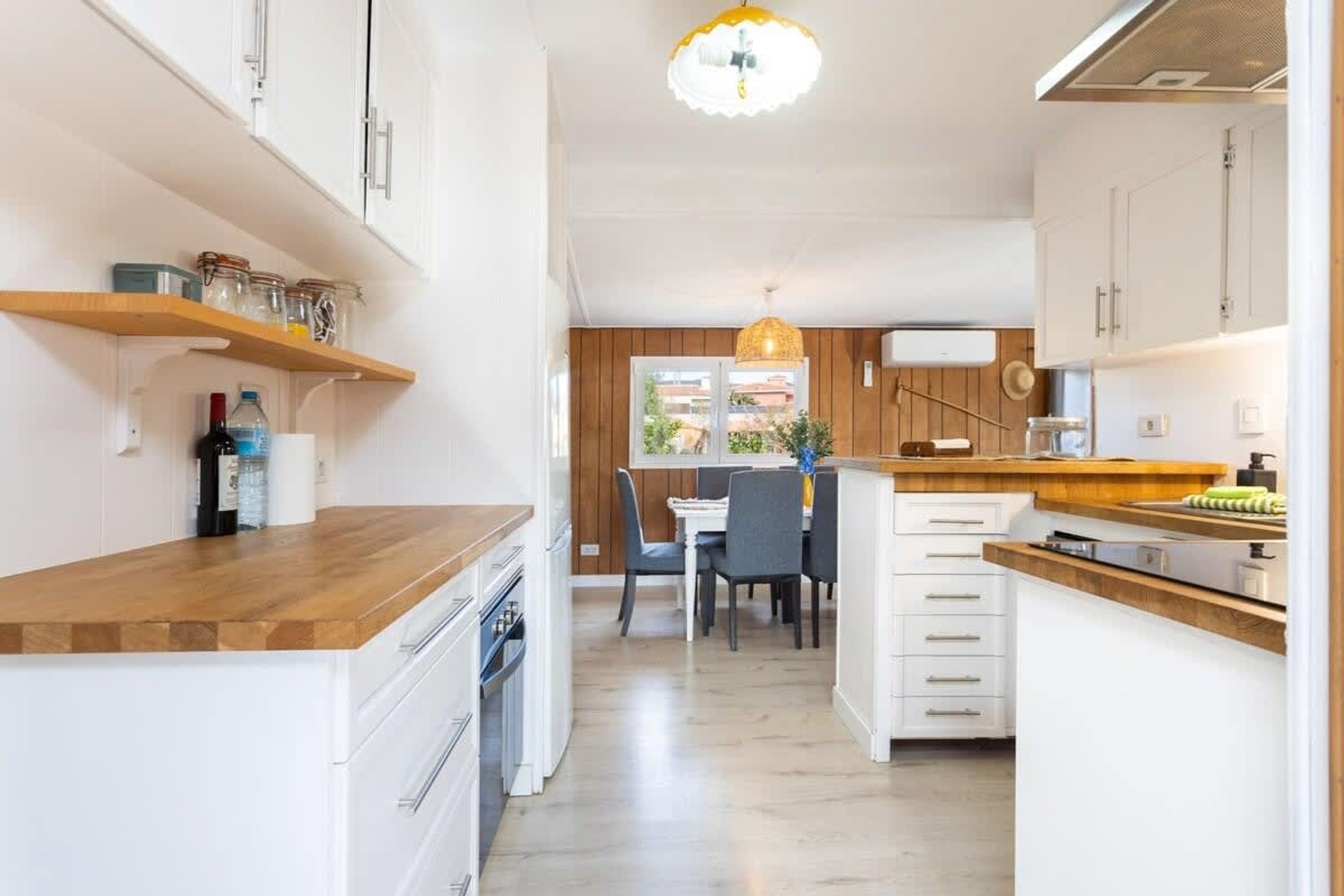 Uma cozinha moderna com bancadas de madeira, armários brancos e um espaço de refeições com mesa e cadeiras.